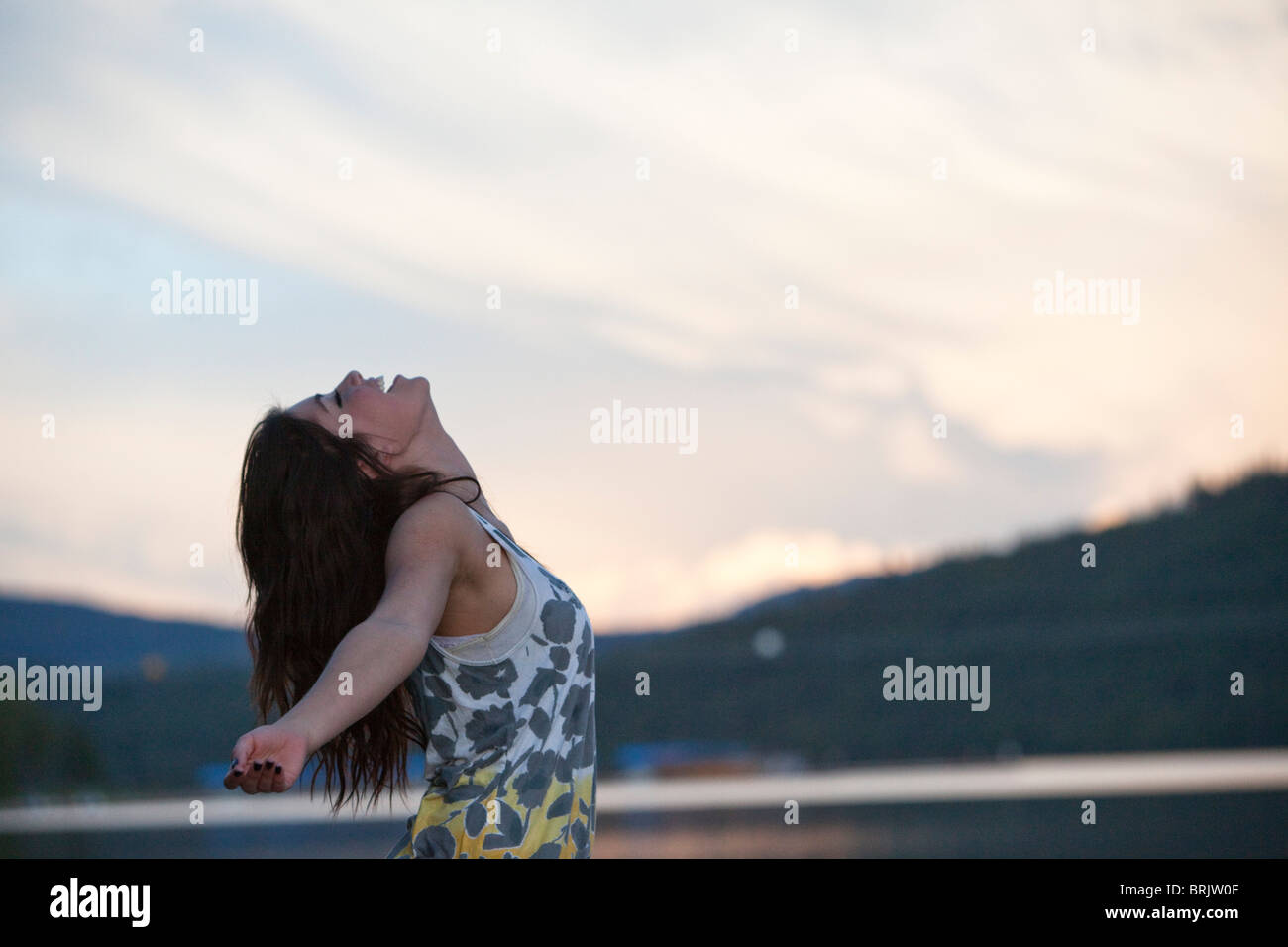 Young woman throws her head back at sunset next to the lake Stock Photo ...