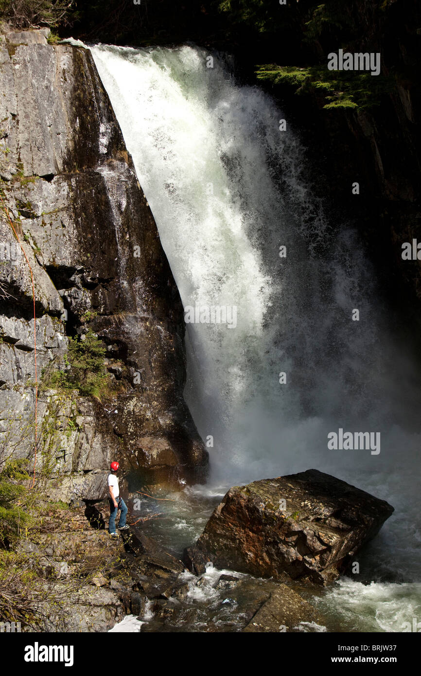 A young man stands at the base of a waterfall looking up Stock Photo ...