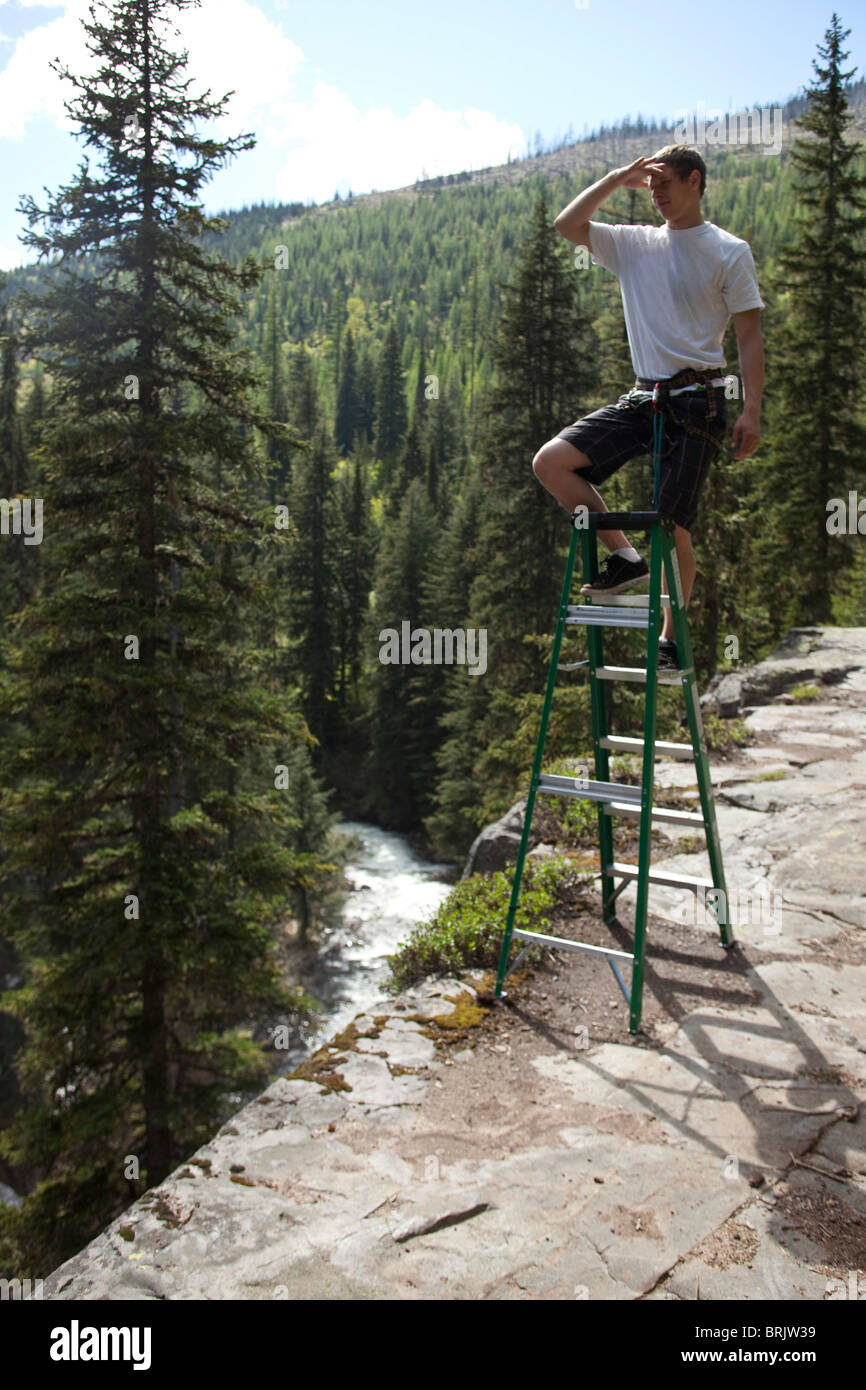 A young man stands on a ladder on the edge of a cliff surveying the ...