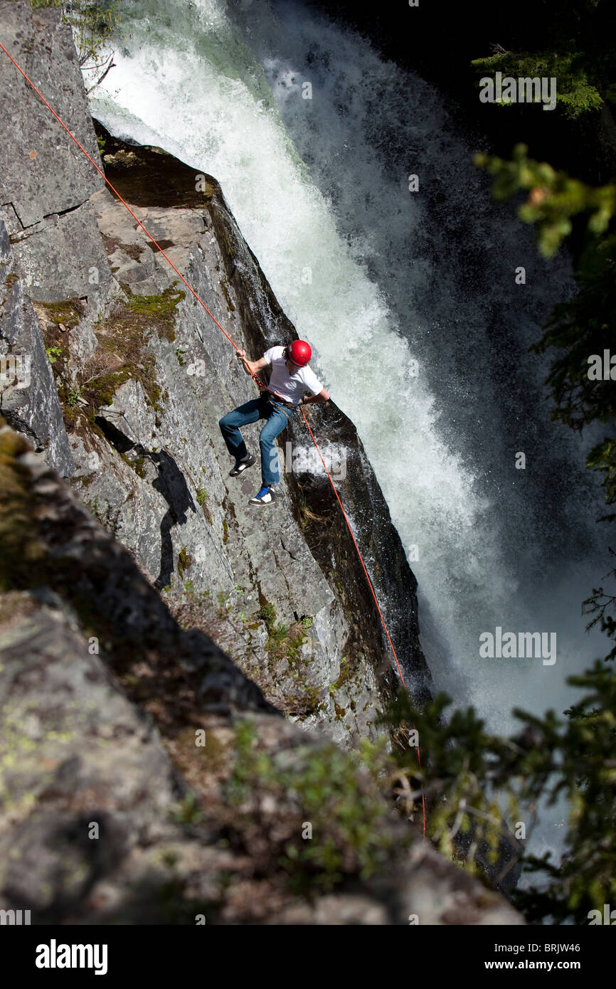 A young man rappels down a cliff next to a waterfall in Idaho Stock ...