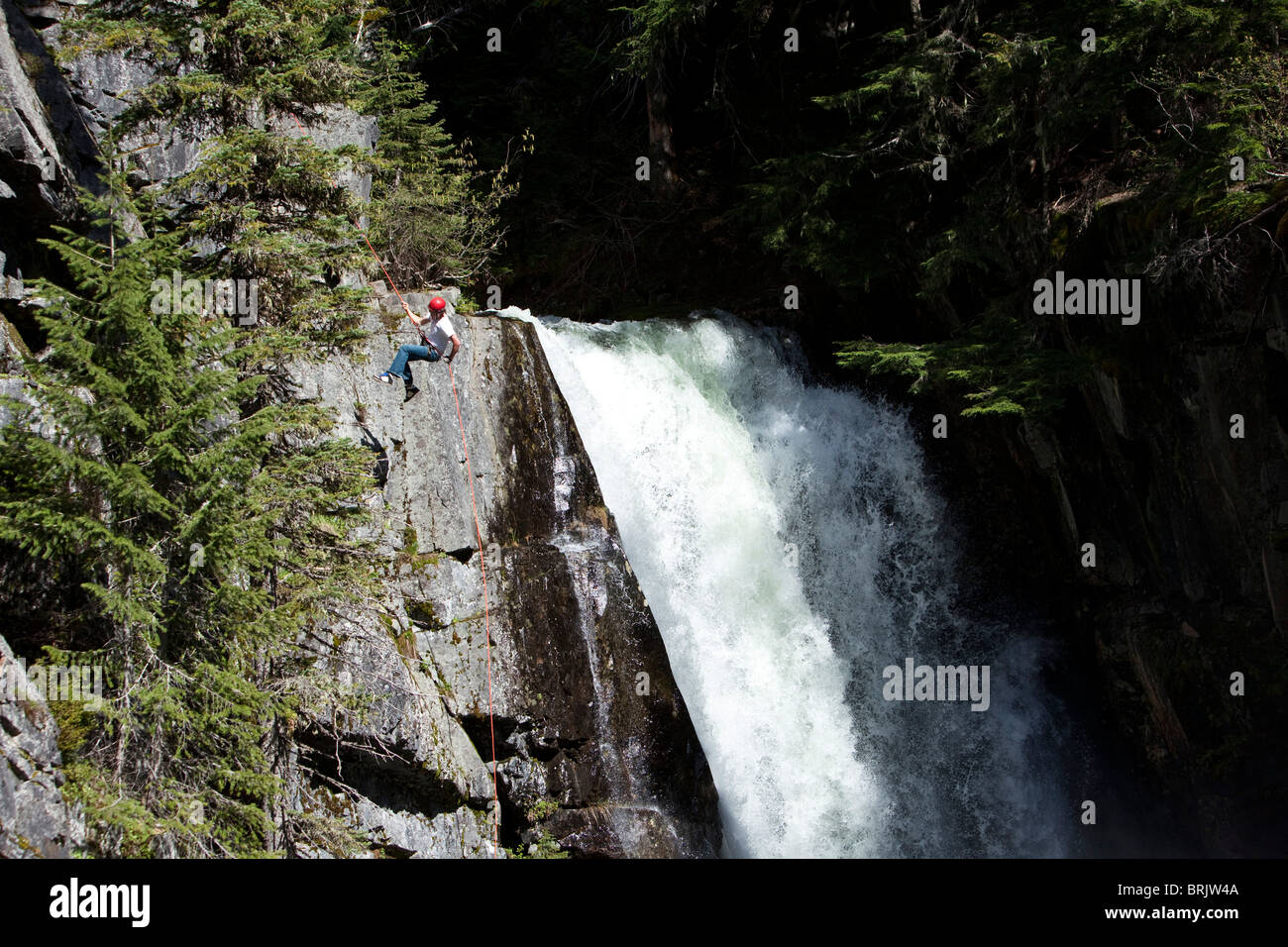 A young man rappels down a cliff next to a waterfall in Idaho Stock ...