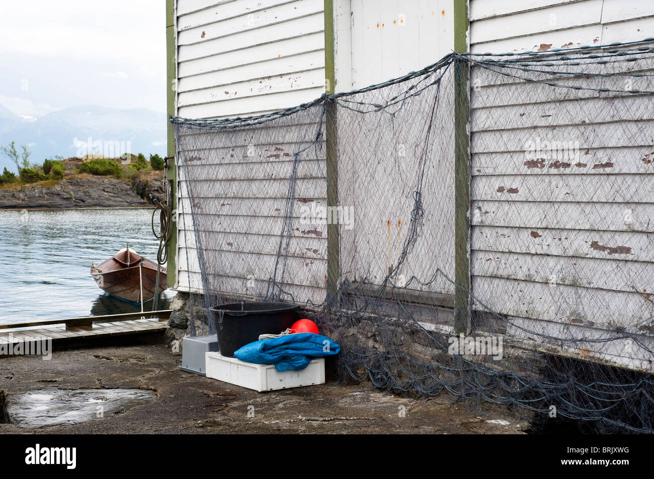 Fishing gear by house wall, with boat in background Stock Photo - Alamy