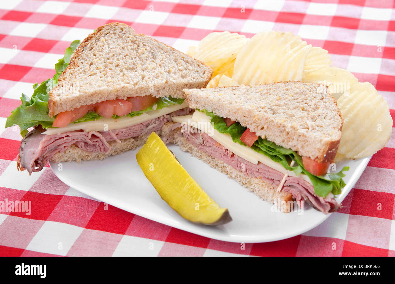 one sliced large roast beef sandwich with a pickle and chips on a white ...