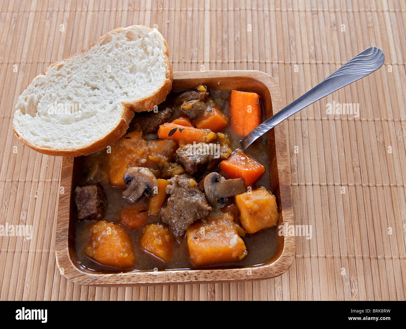 a bowl of rustic beef stew in a wooden bowl with a slice of Italian ...