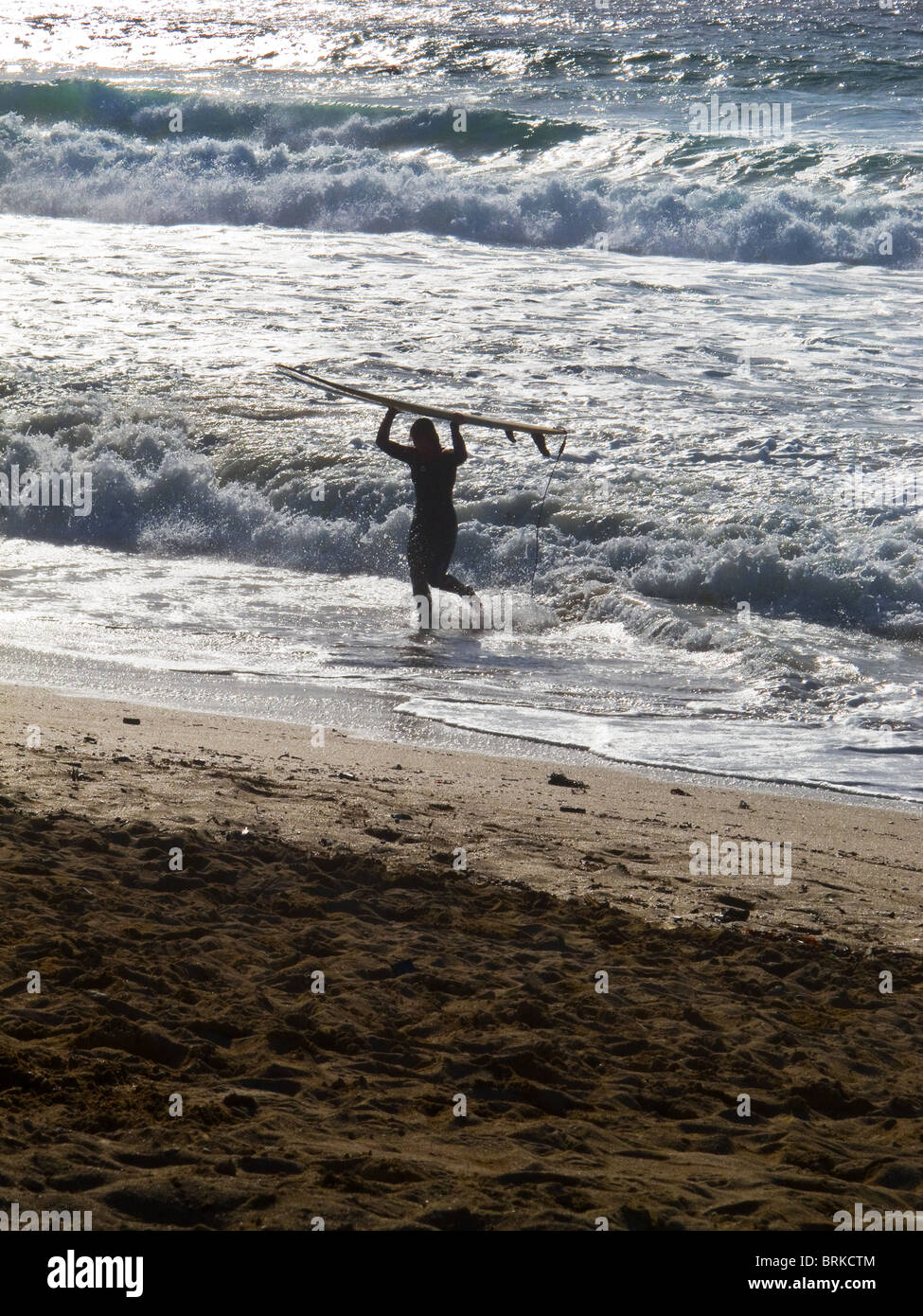 A surfer running through the surf on Fistral Beach in Cornwall. Photo ...