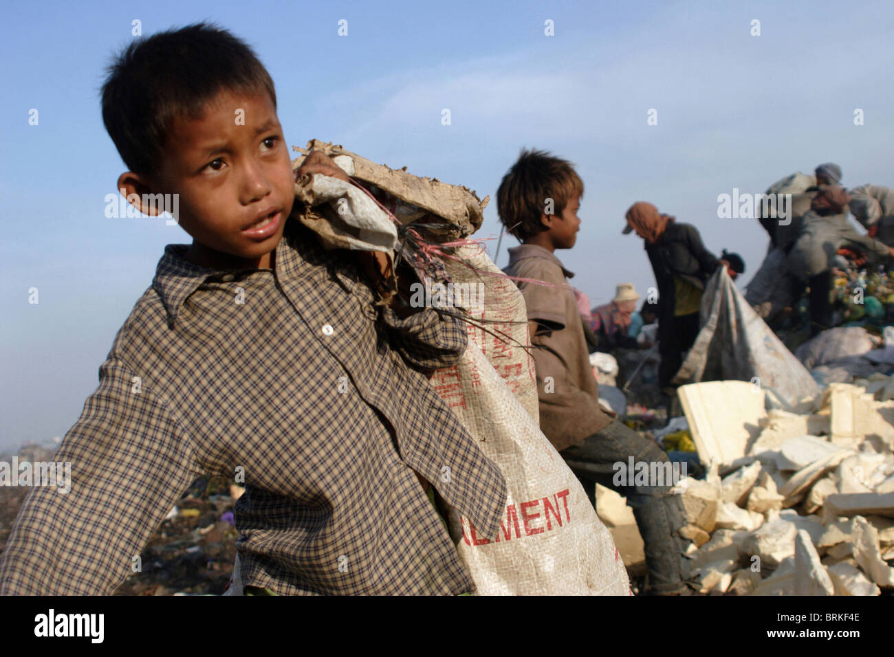 A young child laborer is carrying a big sack filled with garbage at the ...