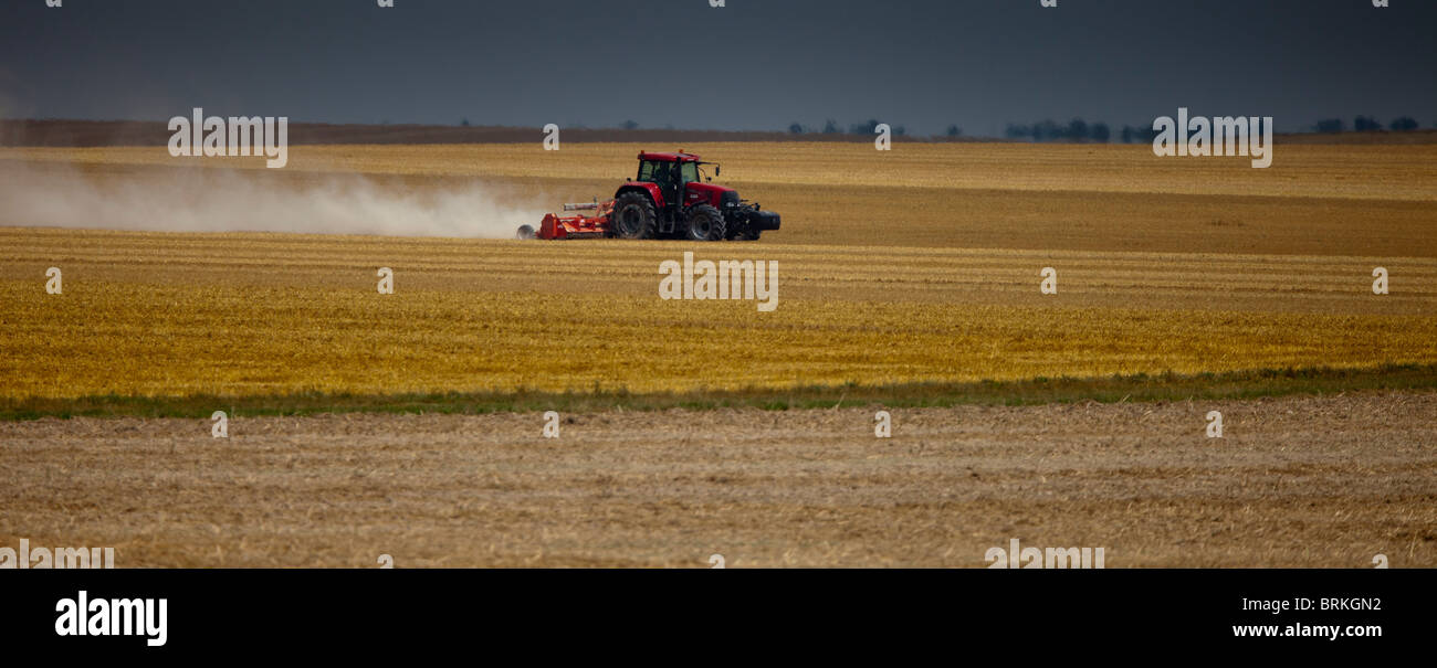Caption Red tractor rotovating a field of straw stubble in France Stock ...