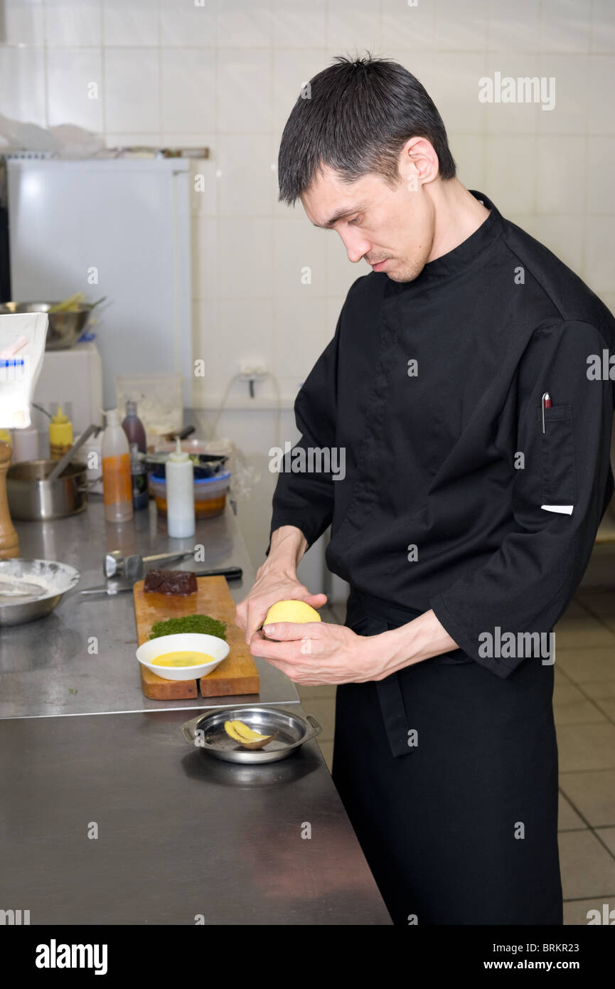 male caucasian chef in black uniform peels a potato Stock Photo - Alamy