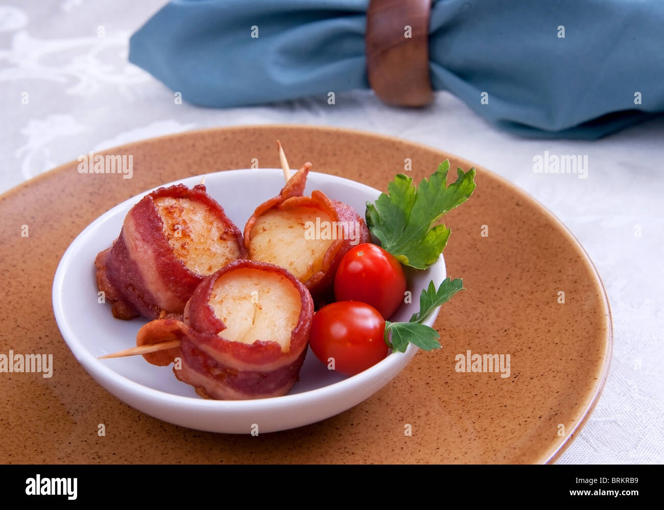 three bacon wrapped scallops in a bowl with tomatoes Stock Photo - Alamy