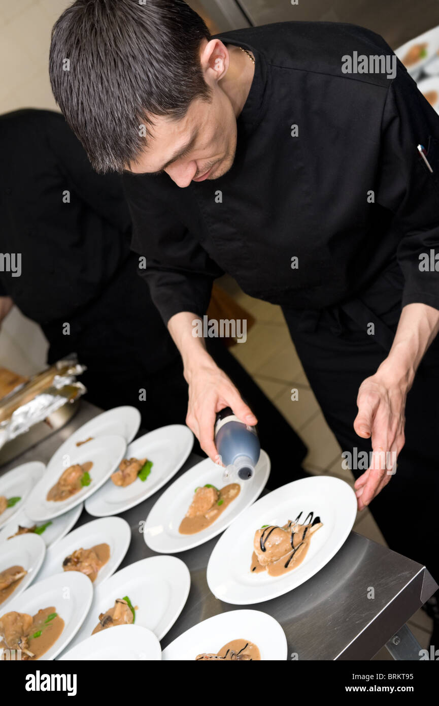 male caucasian chef in black uniform pour sauce on plates with lamb ...