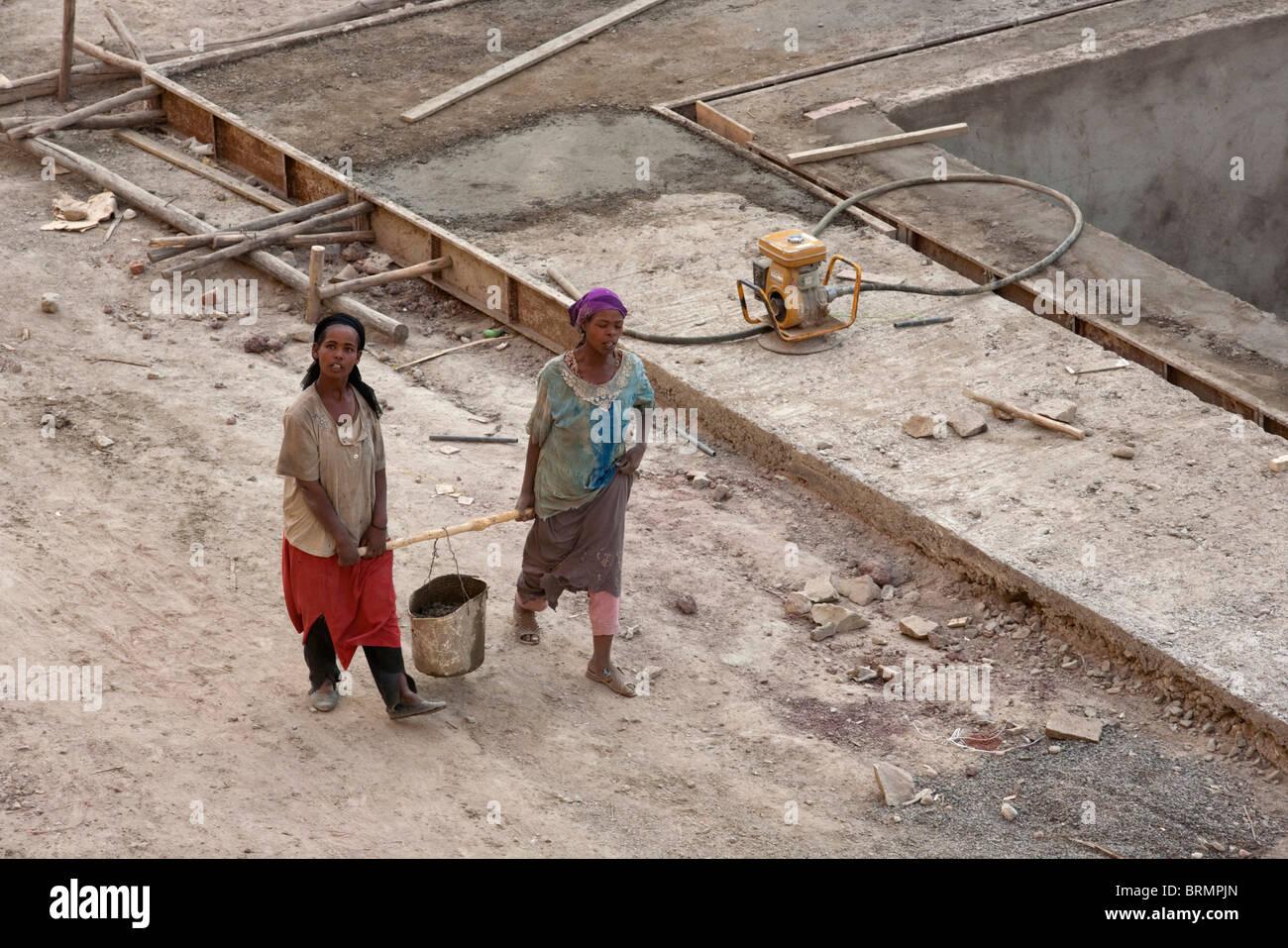Two female construction workers carrying wet cement in a bucket carried ...