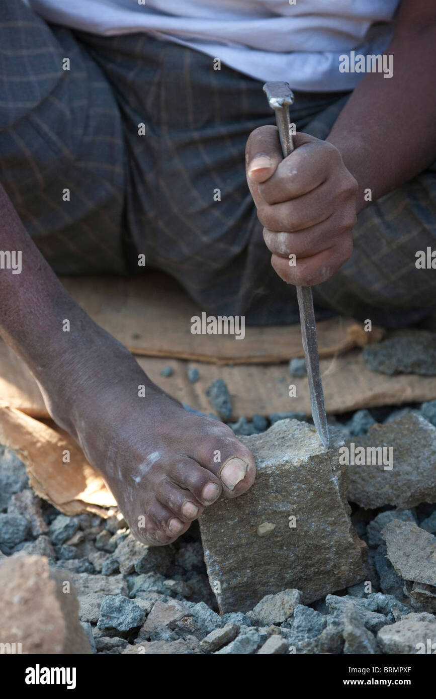 Close-up of a man using a chisel to make a cube-shaped cobble stone ...