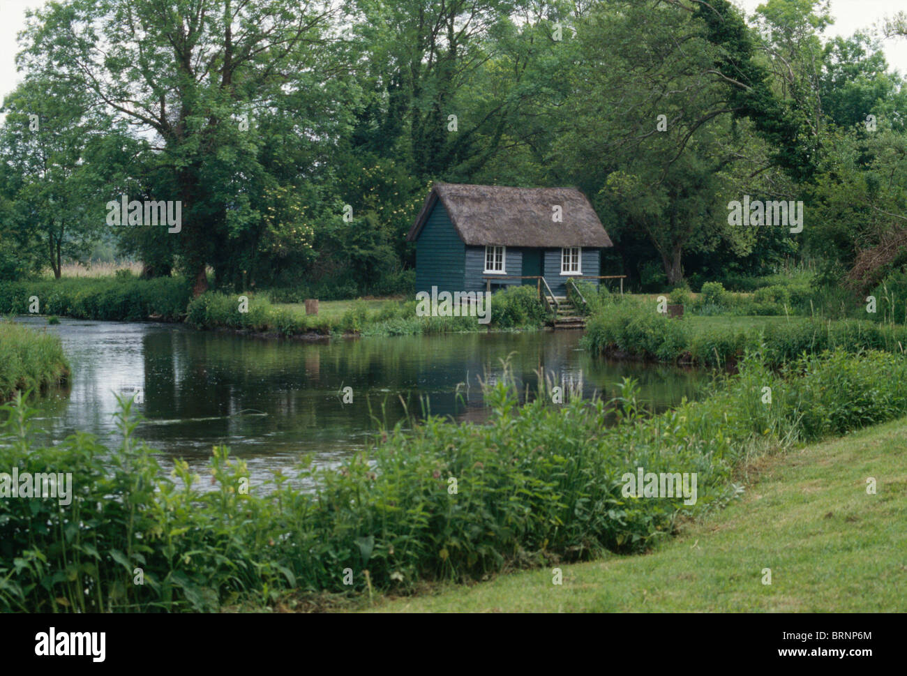 Small green wooden hut on the banks of a river in English countryside ...