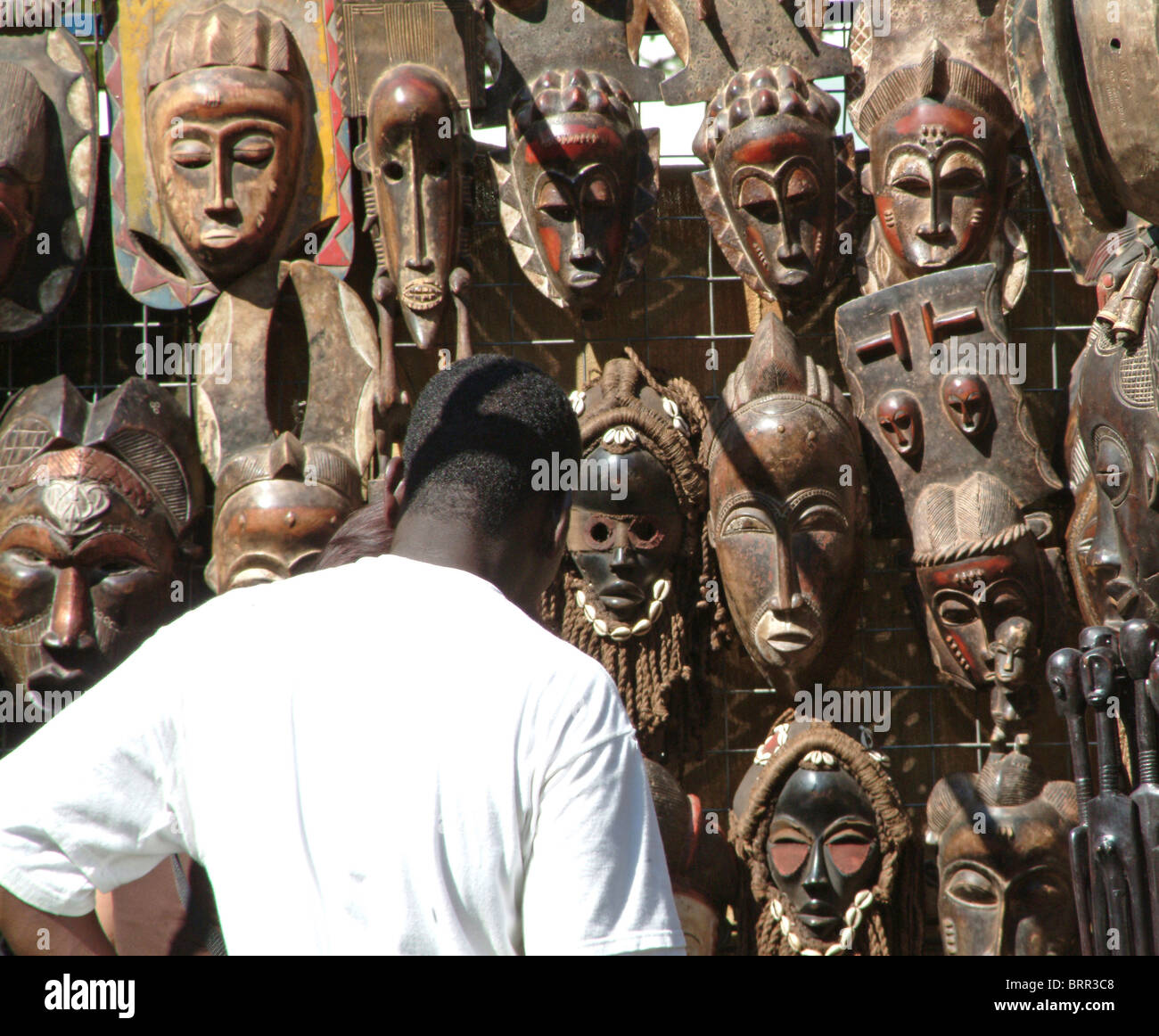 A man looking at display of carved wooden masks at an African flea ...