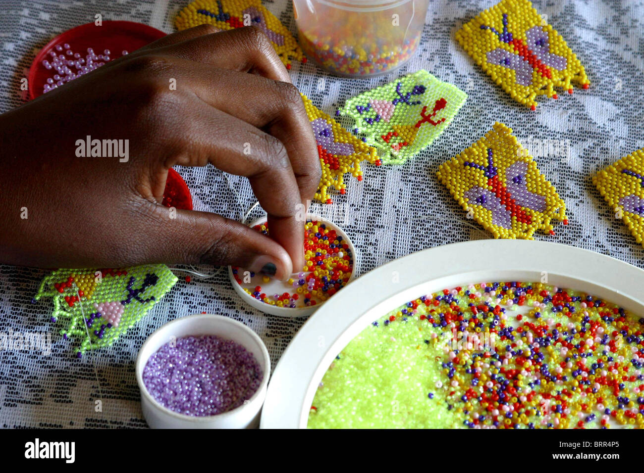Close-up of woman's hand selecting tiny beads and completed beadwork ...