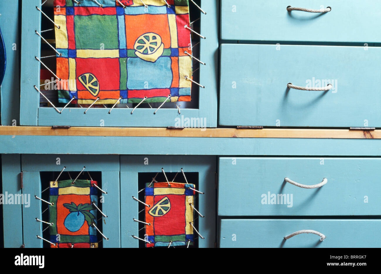 Close-up of pale blue kitchen storage drawers with colorful fabric ...