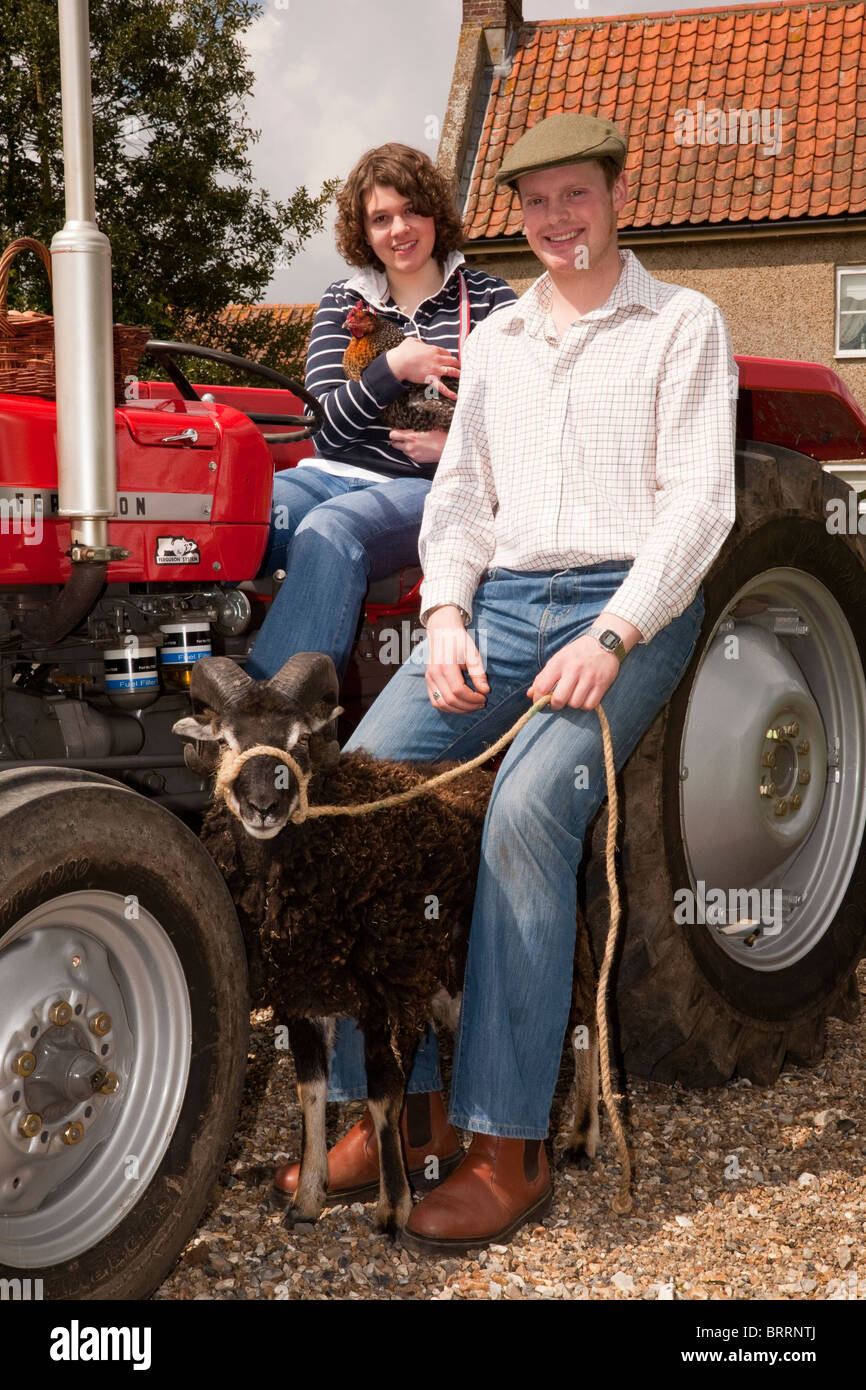 A young farming couple sitting on a tractor outside a farmhouse with a ...
