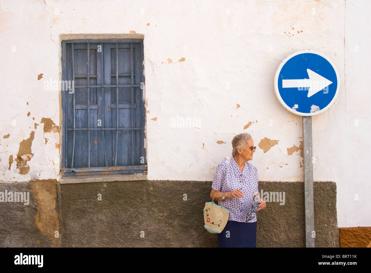 Old lady stood waiting in front of peeling whitewashed wall Stock Photo ...