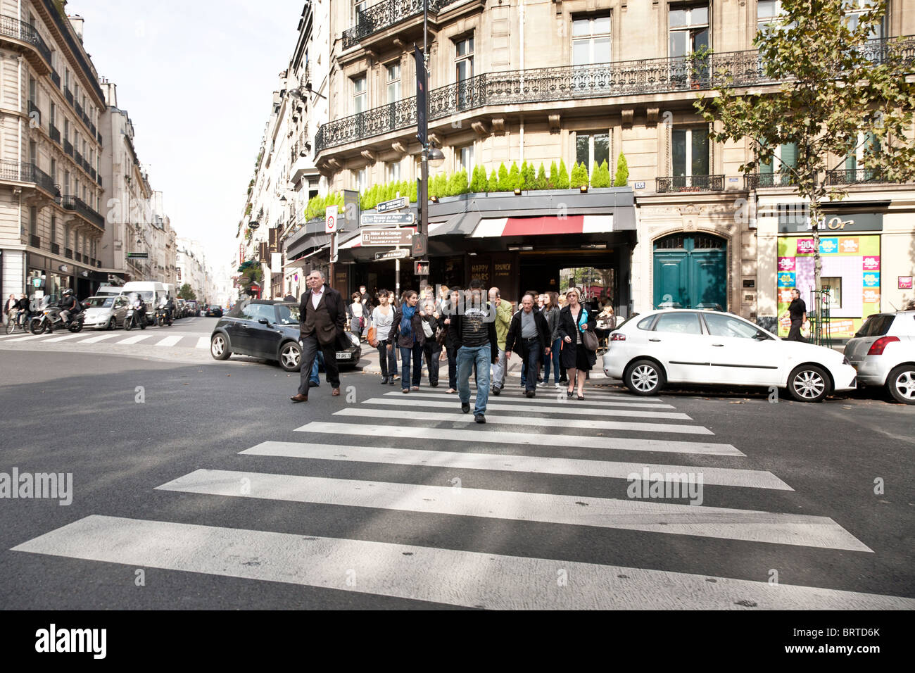 diverse group of Parisian pedestrians hurry across an intersection of ...