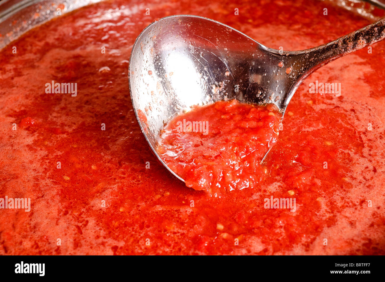 A sunlight steel ladle stirs heated tomato juice in a steel saucepan ...