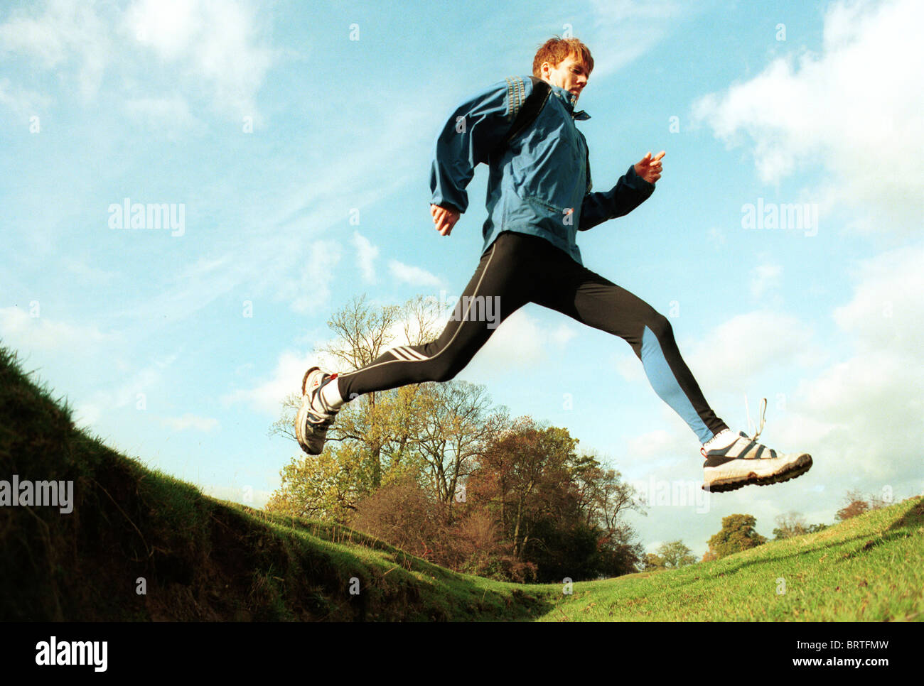 A runner in a country park, leaping over a stream Stock Photo - Alamy