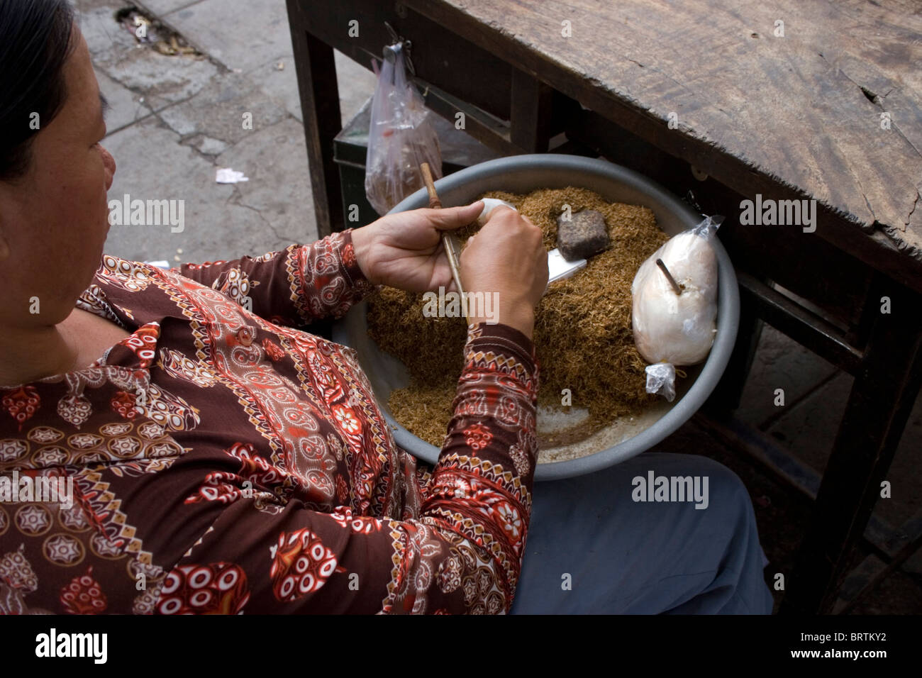 A woman is rolling hand made cigarettes on a sidewalk in Phnom Penh ...