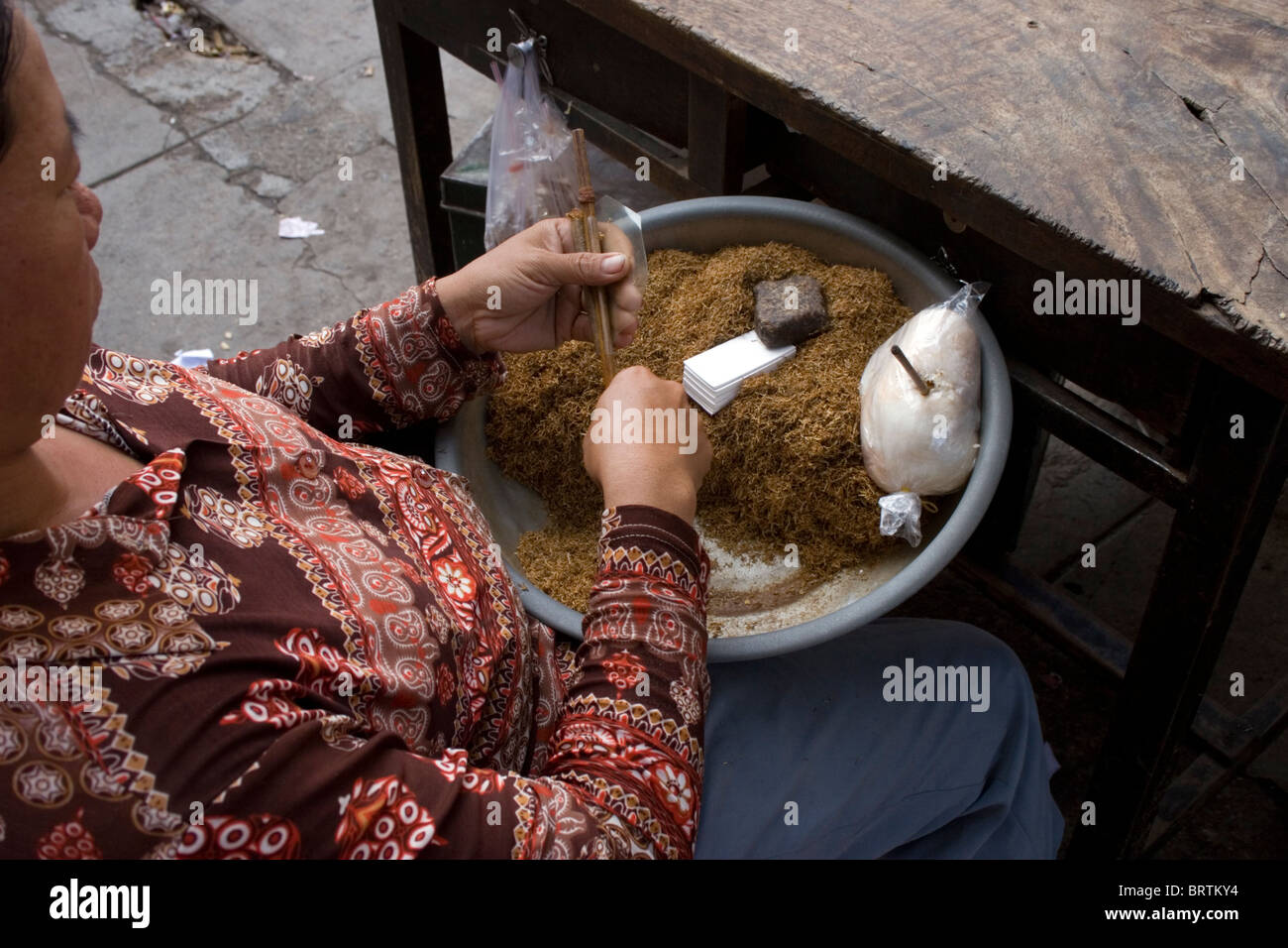 A woman is rolling hand made cigarettes on a sidewalk in Phnom Penh ...