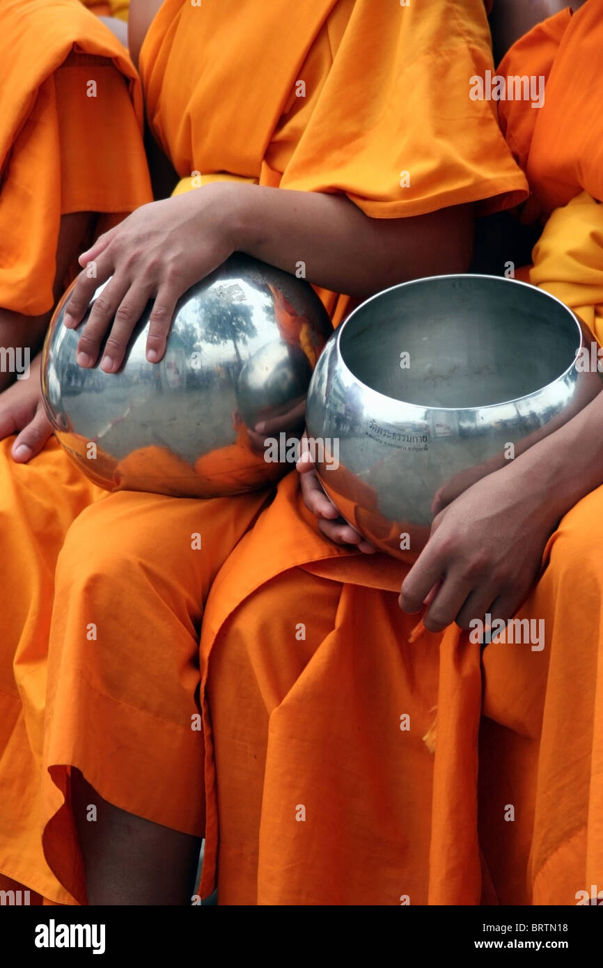 Buddhist monks wearing orange robes sit with their alms bowls near Tha ...