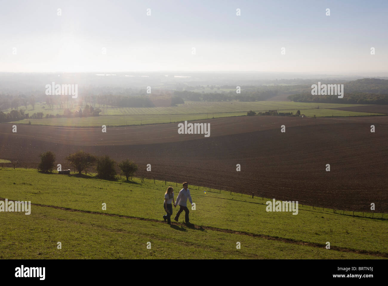 Young couple walk up Hollingbourne Downs with Kent fields below ...