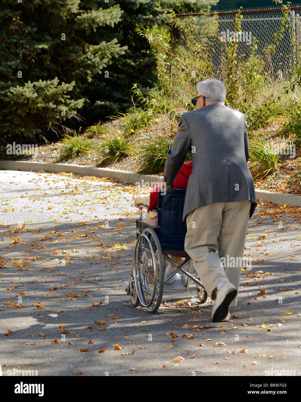 Old man pushing a lady in a wheel chair down a street through late ...
