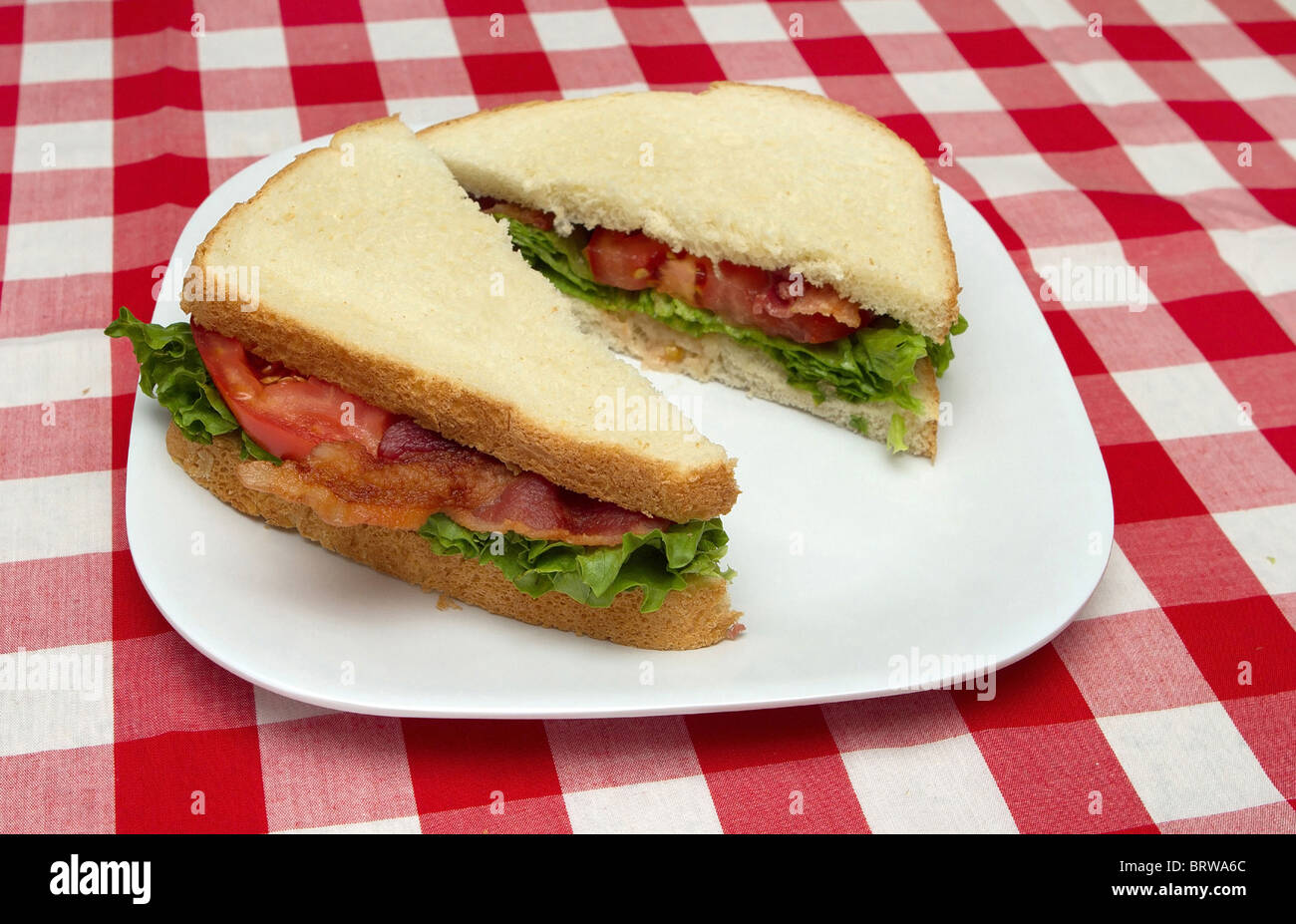 one completed and sliced bacon, lettuce and tomato blt on a white plate ...
