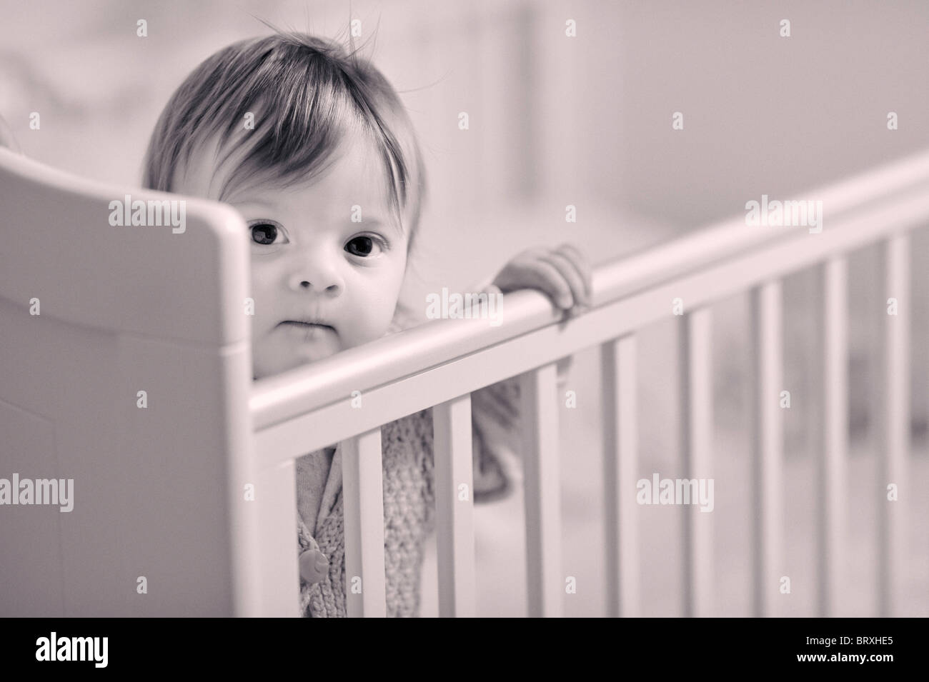 A toddler girl looks innocently from her cot, one hand is resting on a ...