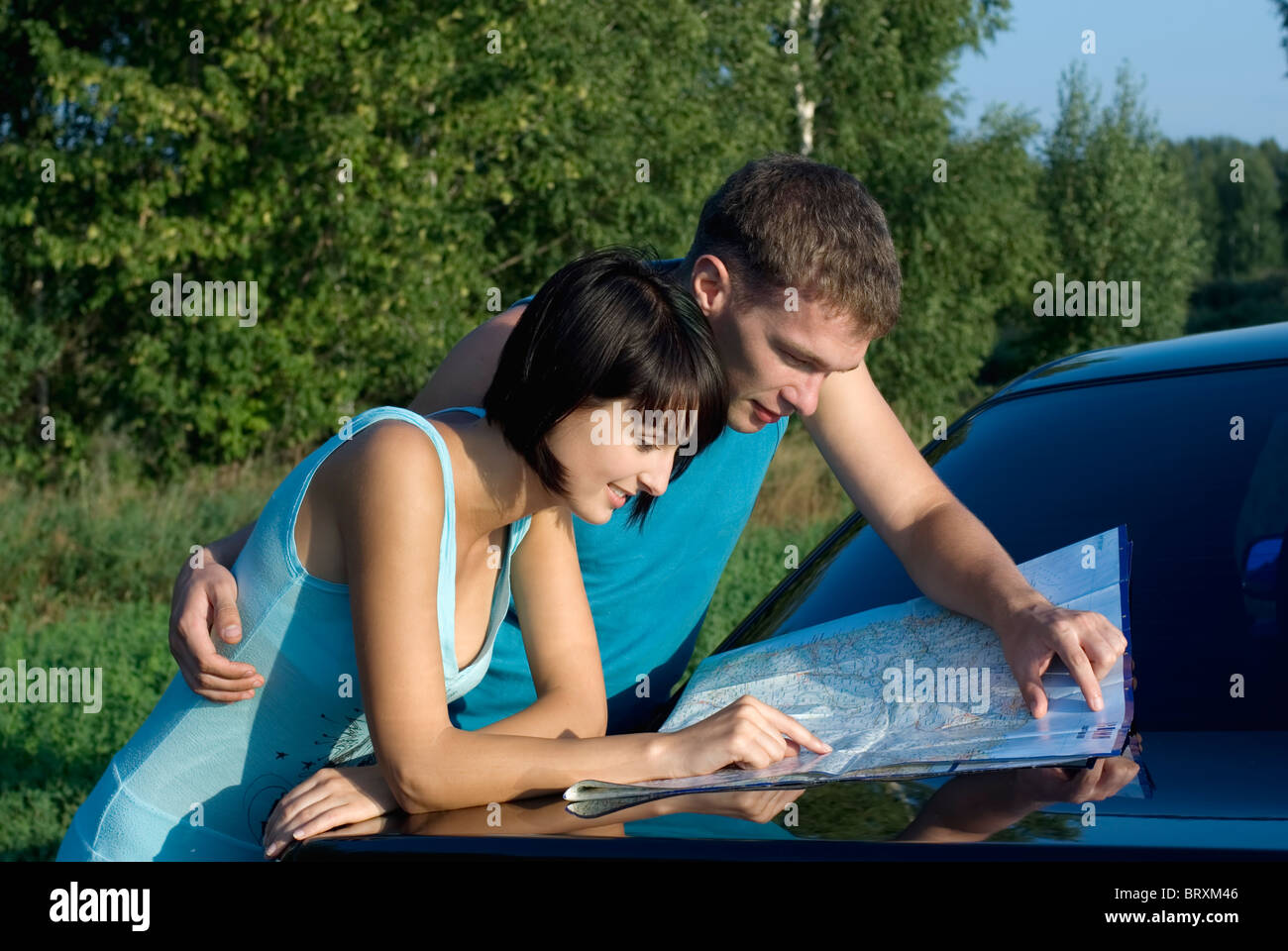 Young man and woman reading map on hood of car Stock Photo - Alamy