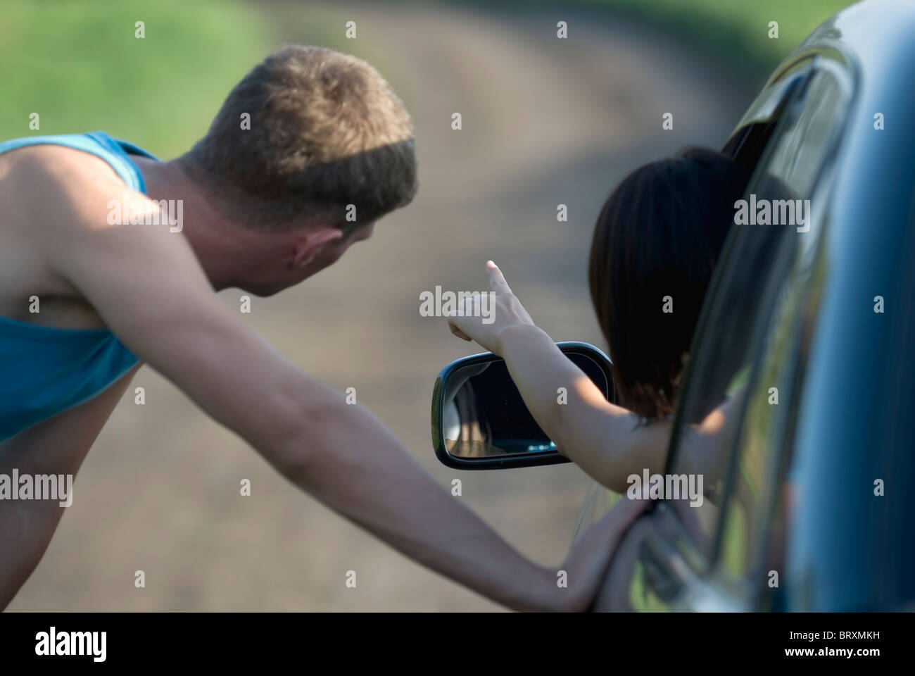 Young woman pointing from car with young man leaning to car Stock Photo ...