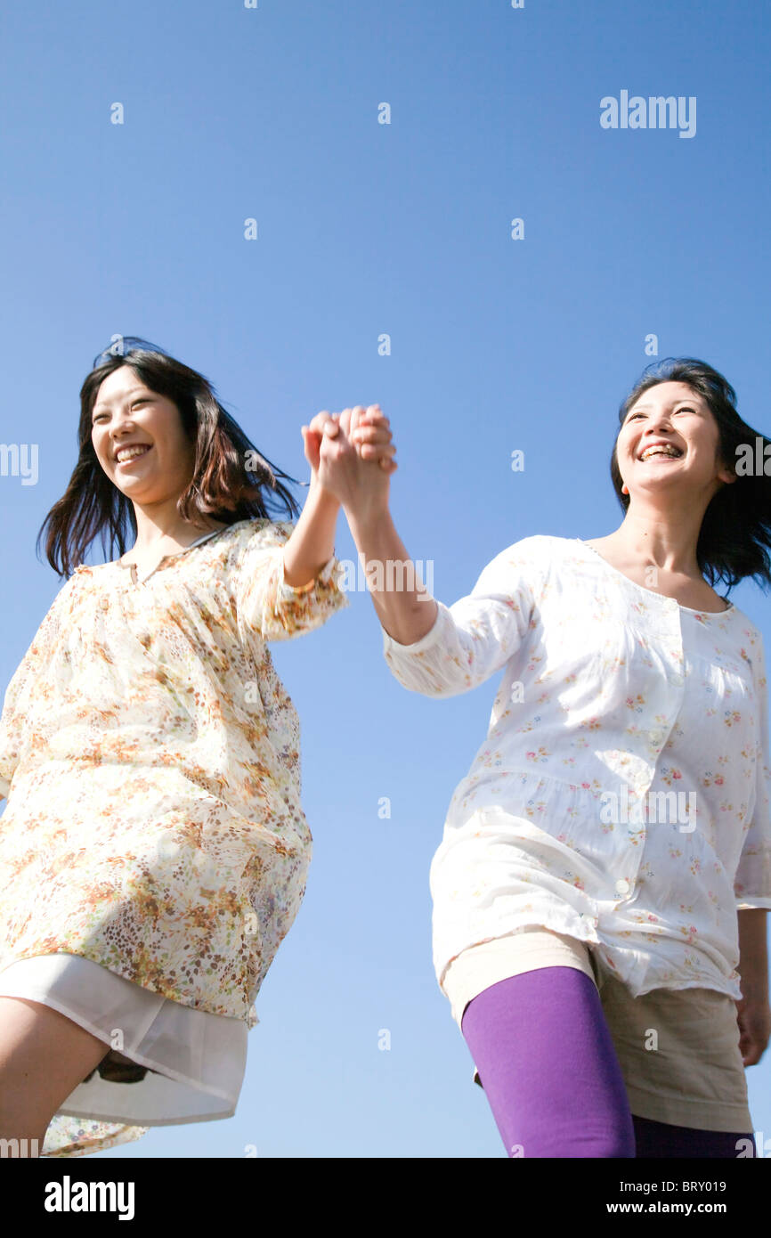 Two Young Women Holding Hands and Jumping Stock Photo - Alamy
