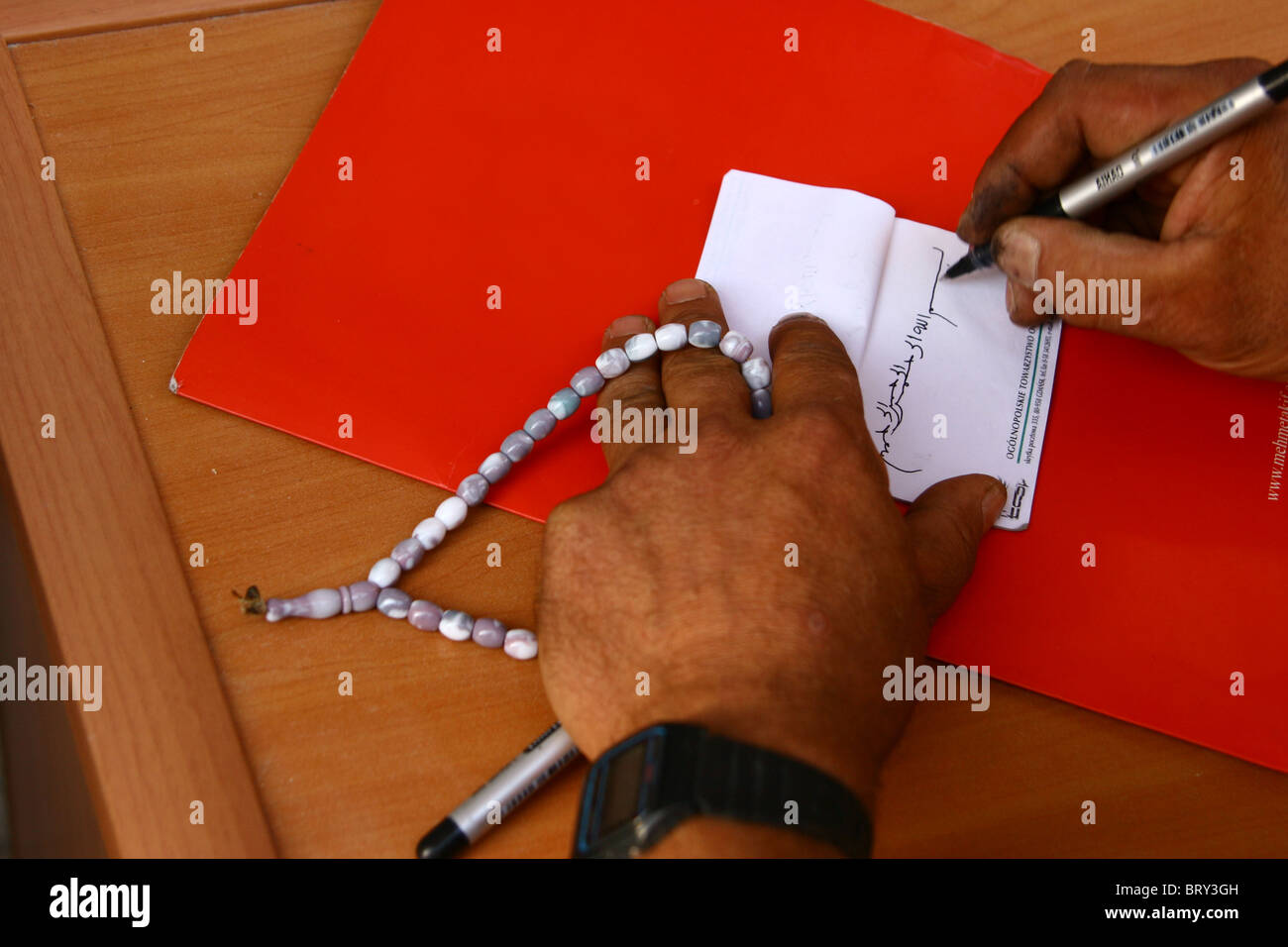 Imam writing God's name in Arabic holding a rosary Stock Photo - Alamy