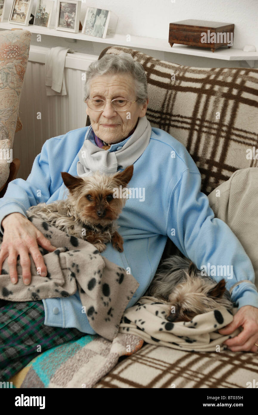 elderly woman keeping warm in winter wrapped up with rugs with her pet ...