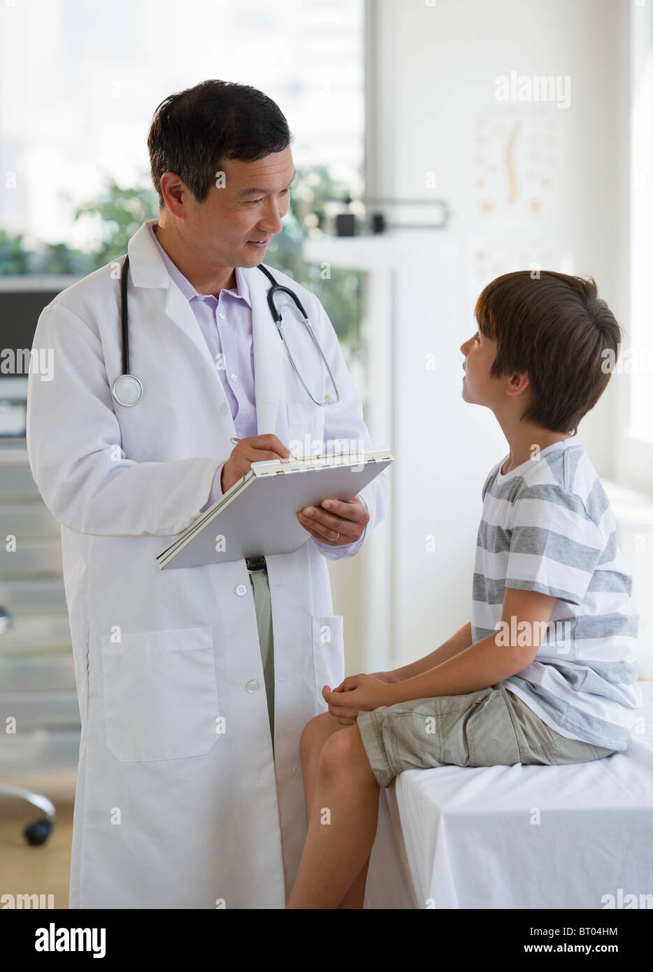 Doctor with medical chart talking to boy in examination room Stock ...