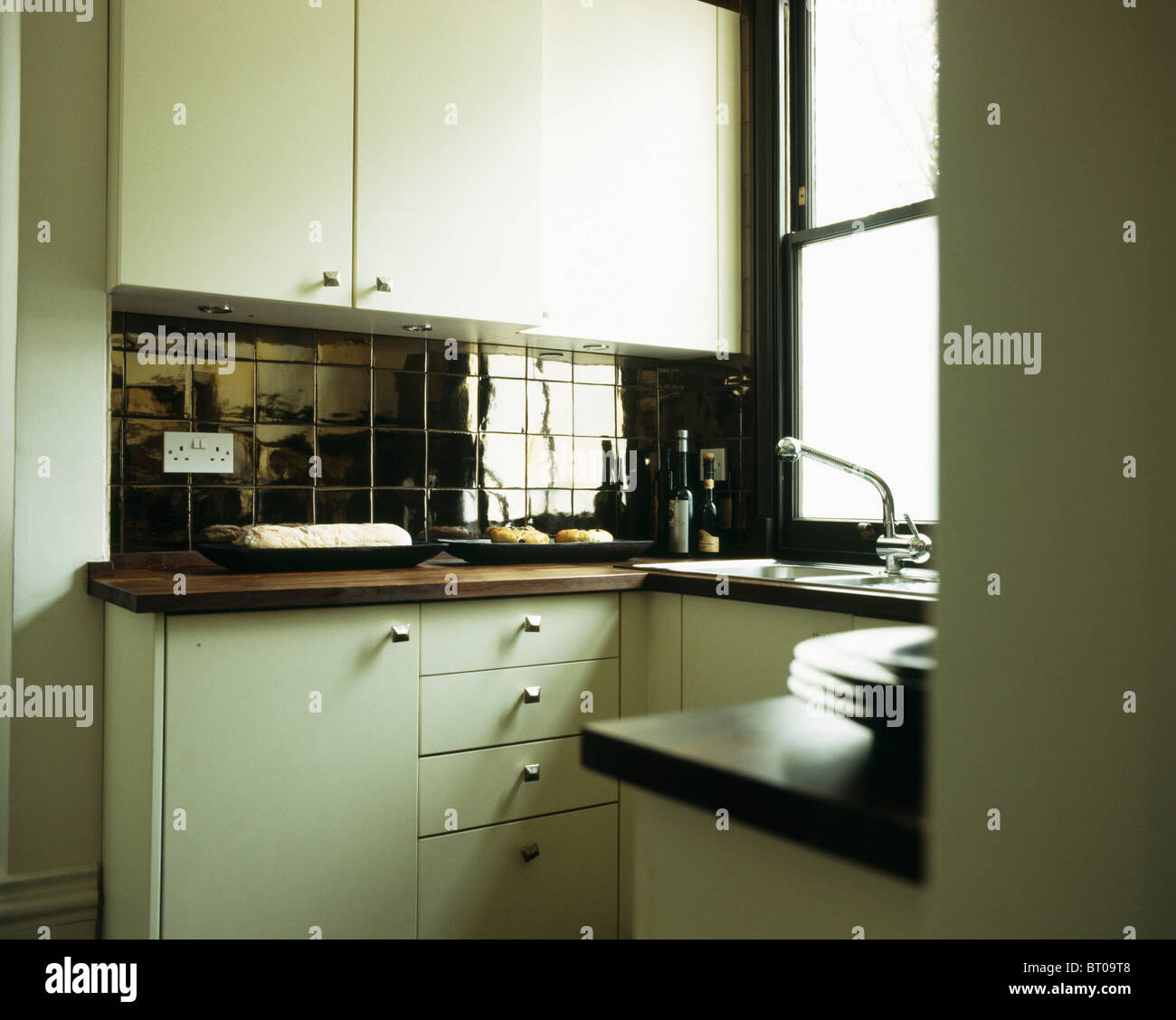Corner of townhouse kitchen with beige fitted units and black tiled ...
