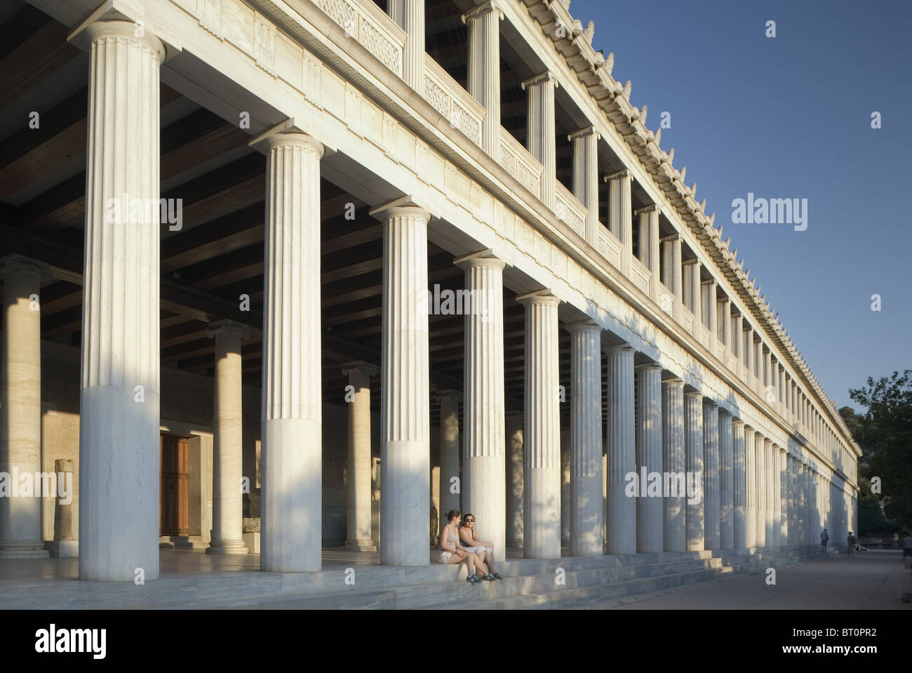 Athens, Greece. Tourists sit on the steps of Stoa of Attalos (or ...