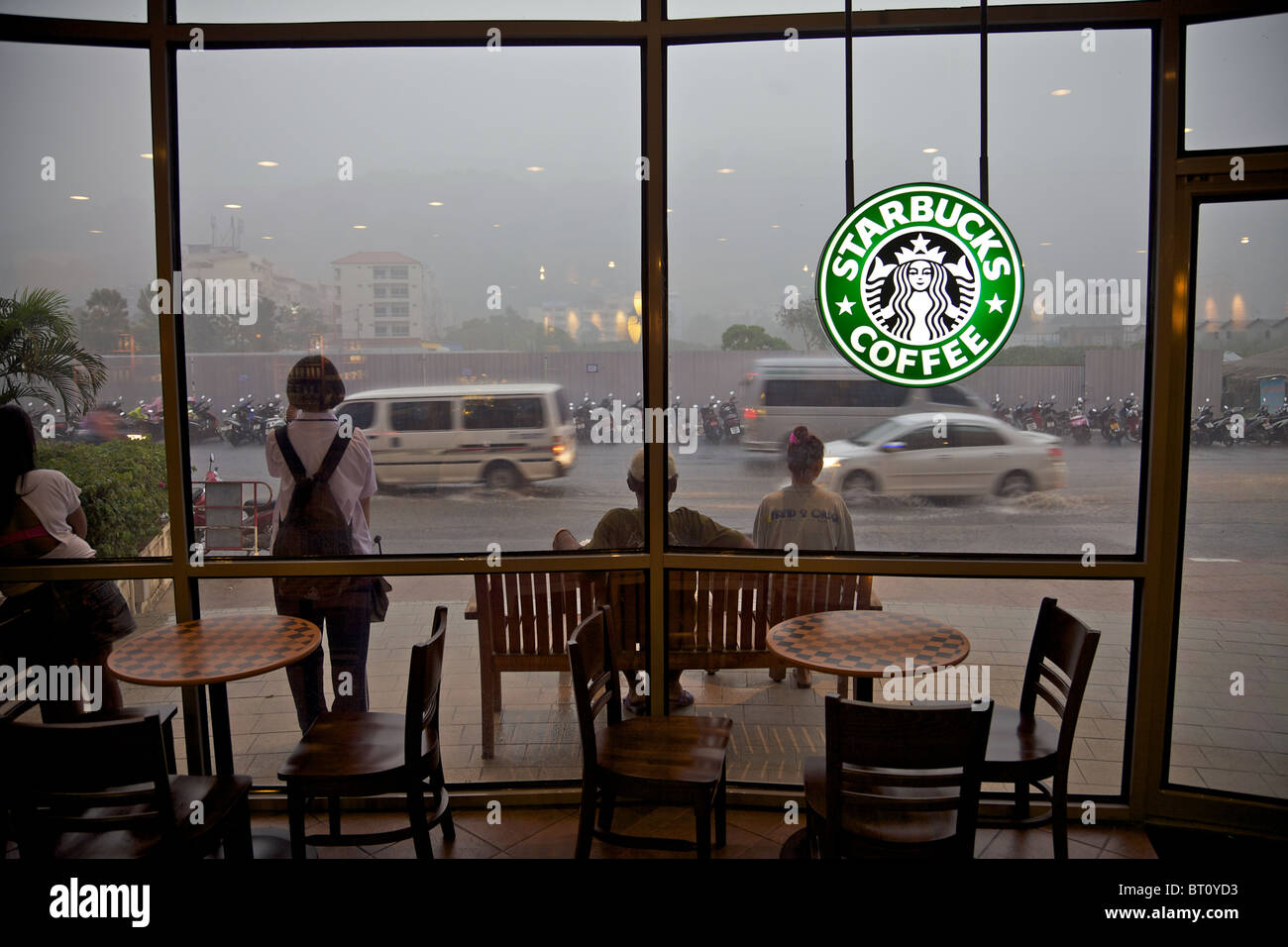 Thai people waiting for the heavy rain to stop outside a Starbucks ...