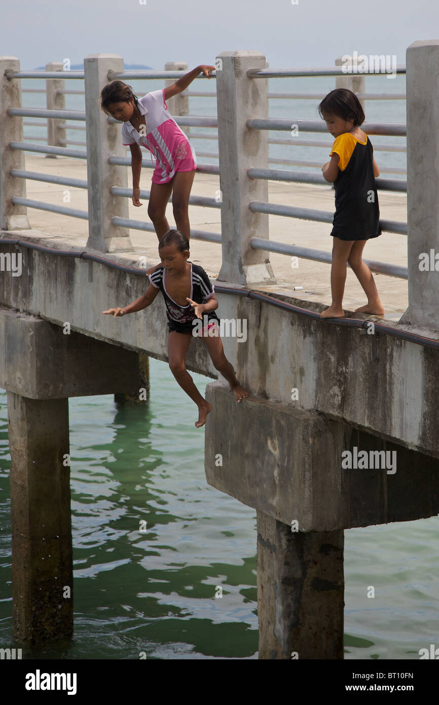 Little girls jumping into the sea from a pier at Rawai, Phuket Thailand ...