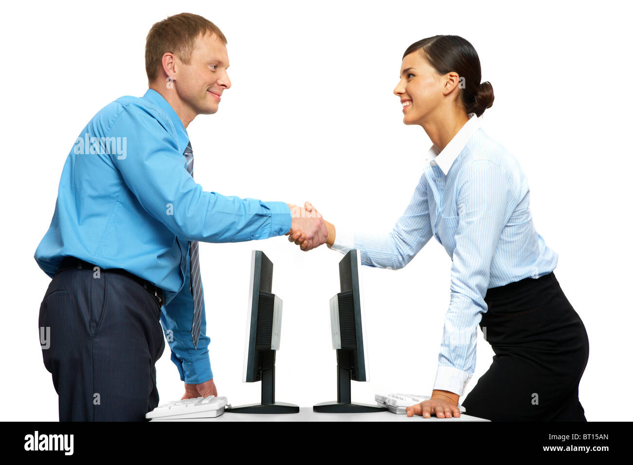 Two businesspeople shaking hands standing at two identical tables with ...