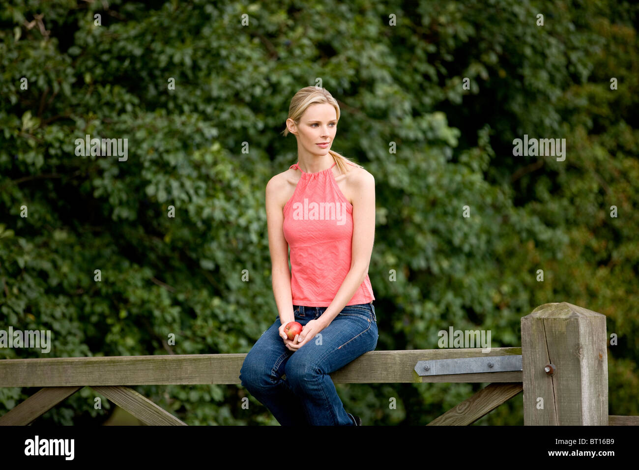 A woman sitting on a gate, holding an apple Stock Photo - Alamy
