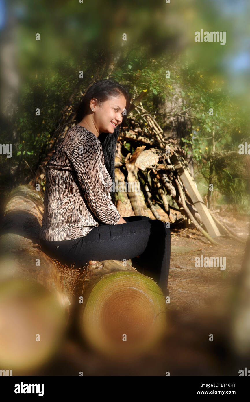 smiling young woman sitting on top of logs in forest Stock Photo - Alamy