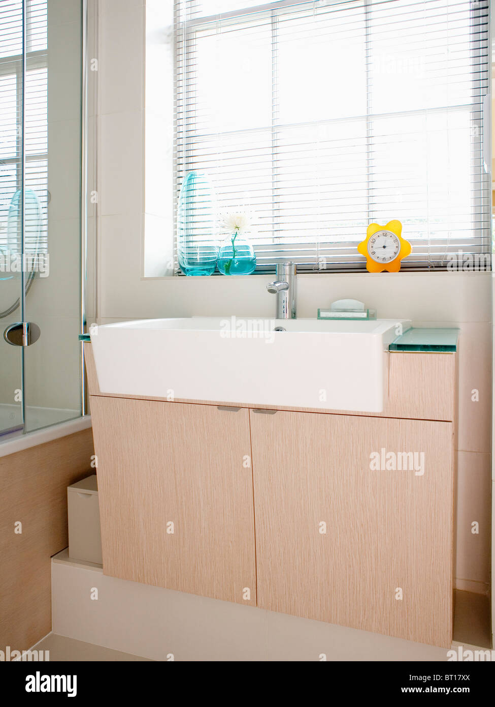 Rectangular white basin in pale wood fitted unit below window with ...