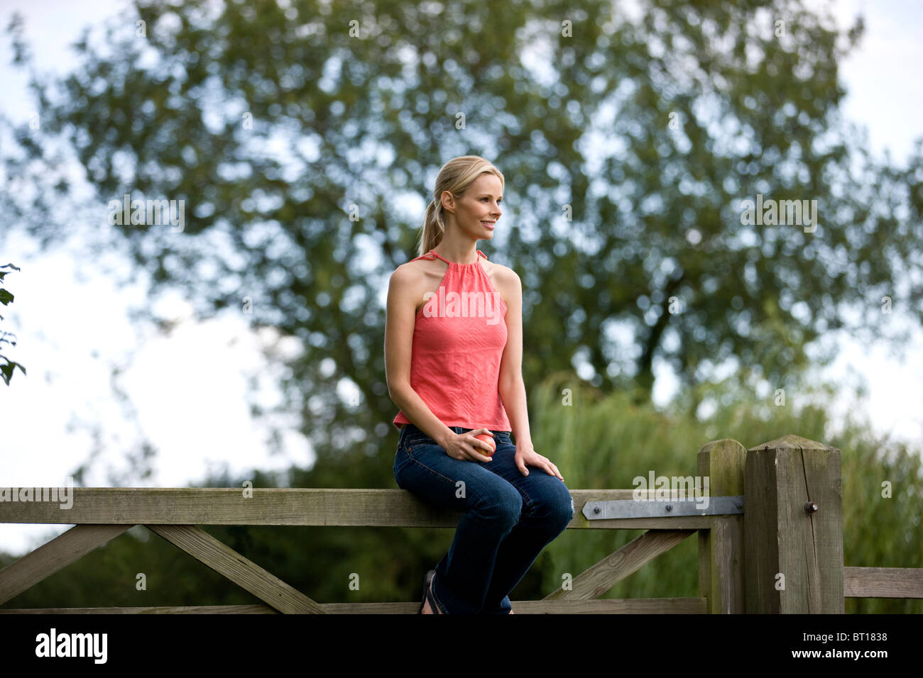 A woman sitting on a gate, holding an apple Stock Photo - Alamy