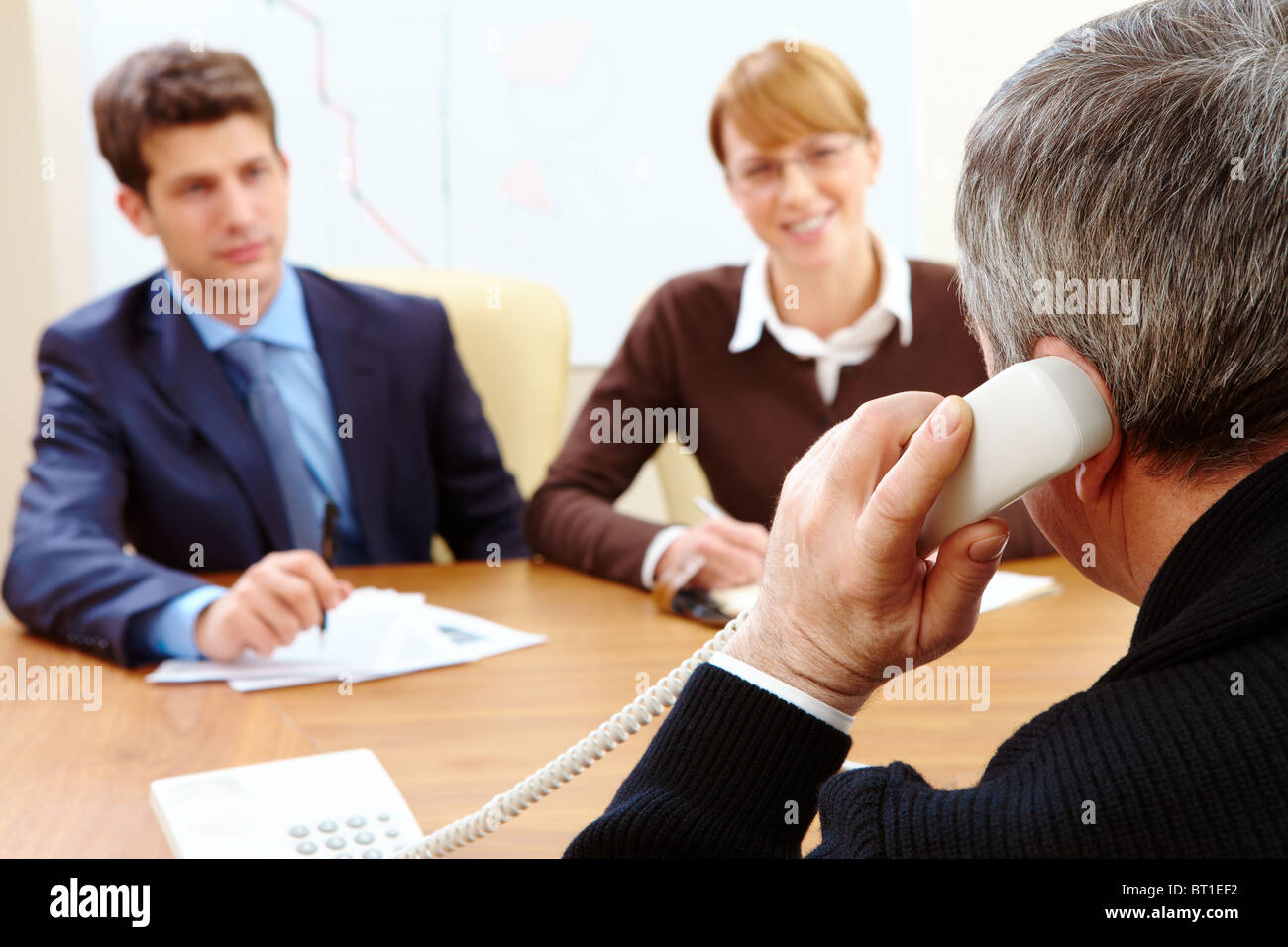 Rear view of bank employee calling on the phone opposite two visitors ...