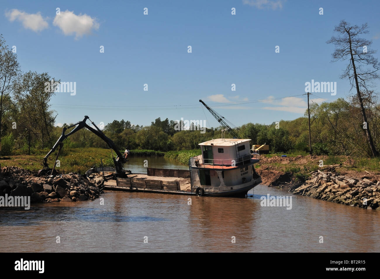 Barge with a grab crane operated by a man repairing river bank rock ...