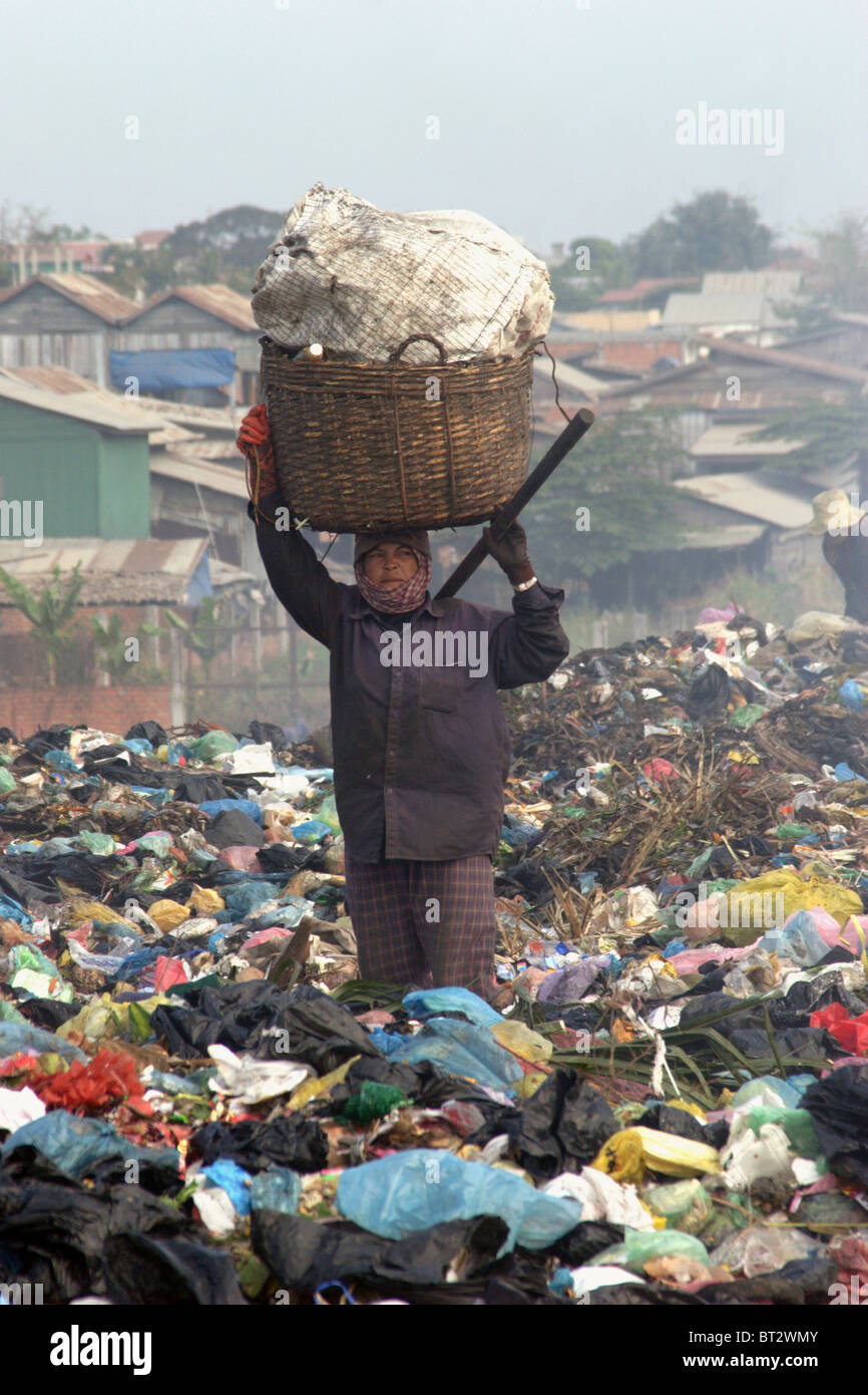 A woman worker is carrying a basket of trash on top of her head at a ...